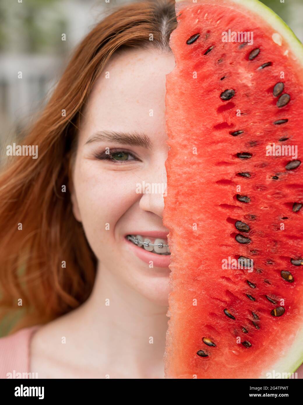 Beautiful red-haired woman smiling with braces on her teeth covers half ...
