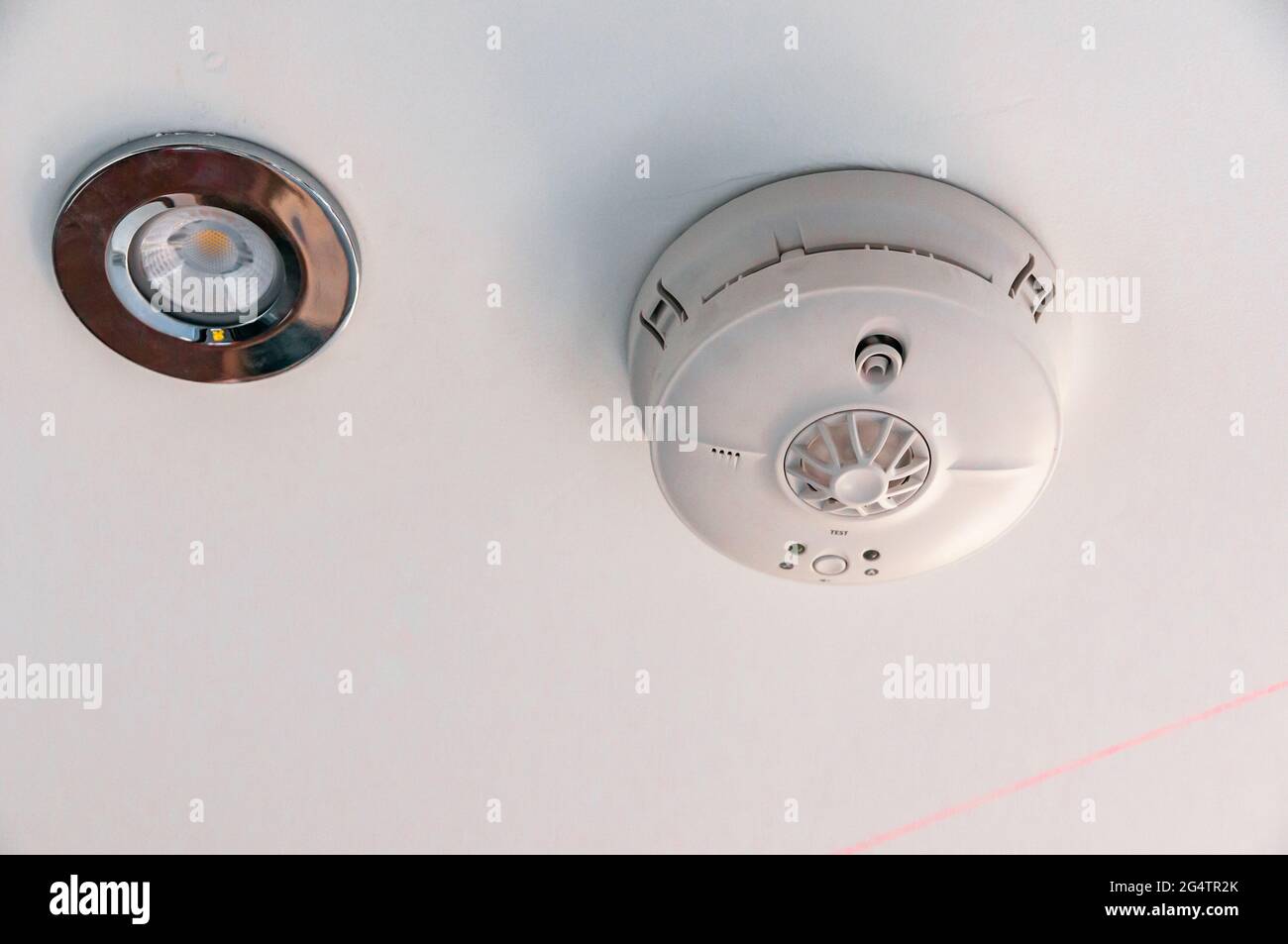A smoke detector alarm is mounted on a white kitchen ceiling next to an ...