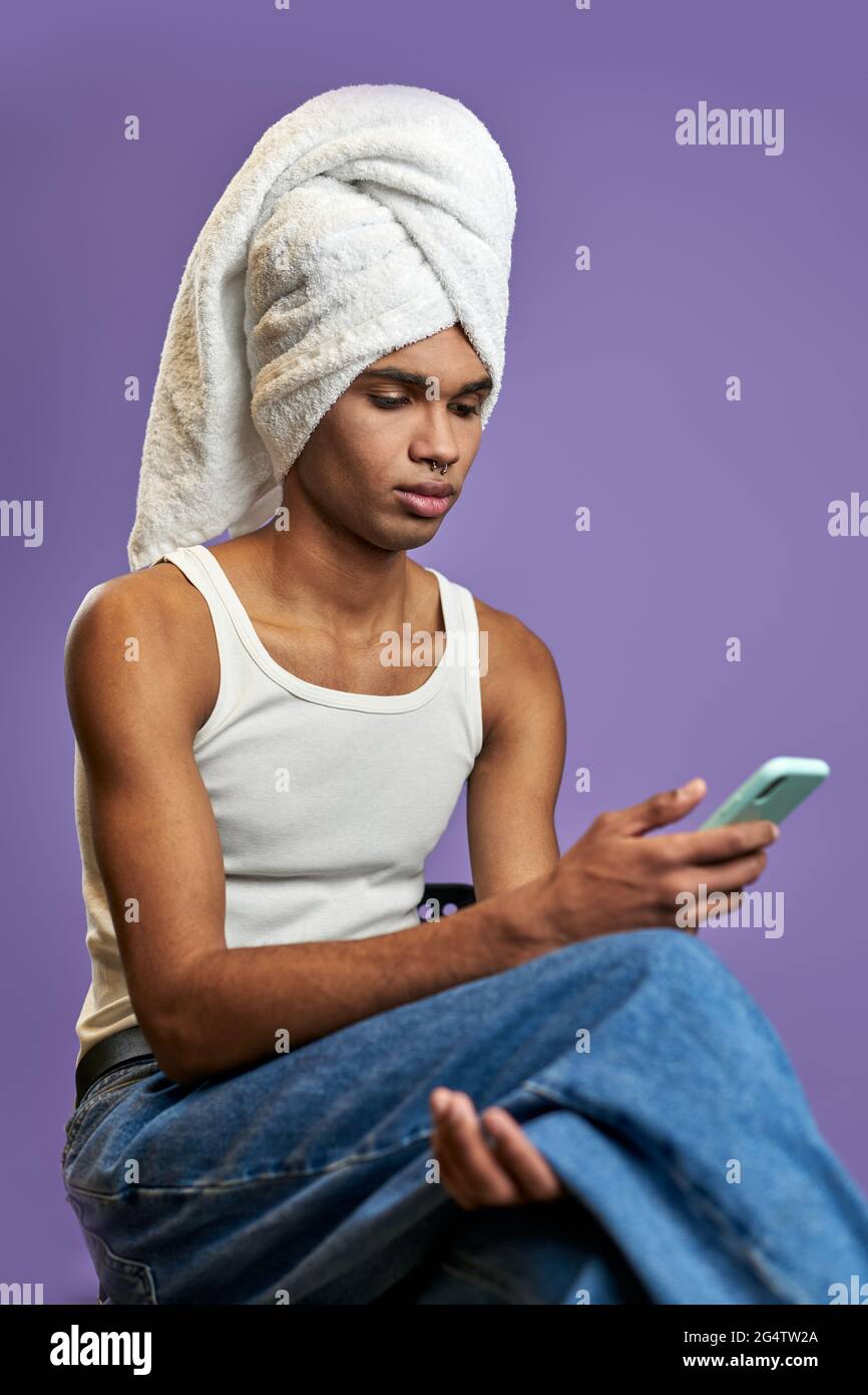Young transgender man in towel looks mobile screen portrait. Muscular ...