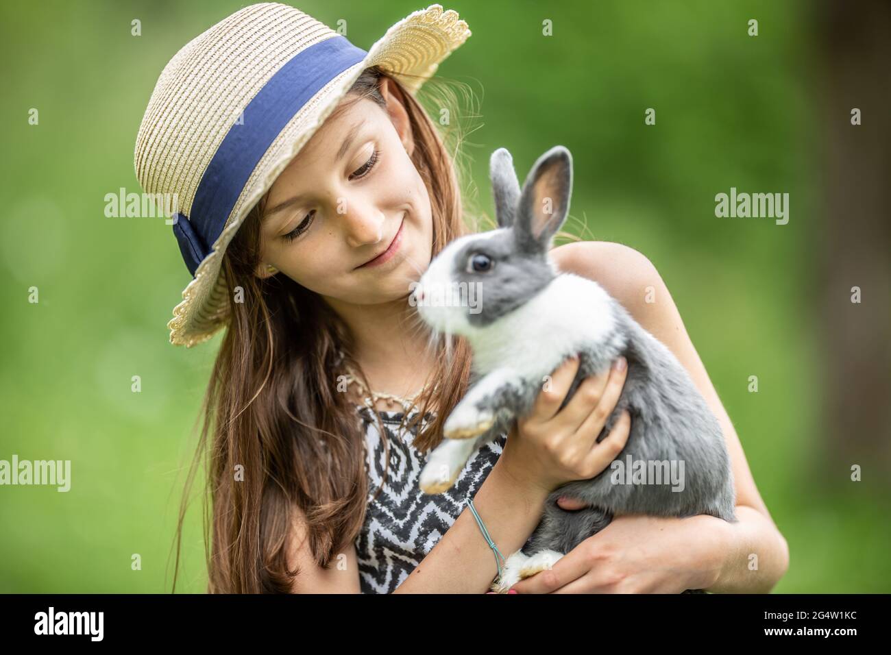 Young kid happily holding a grey rabbit in hands and playing with it ...