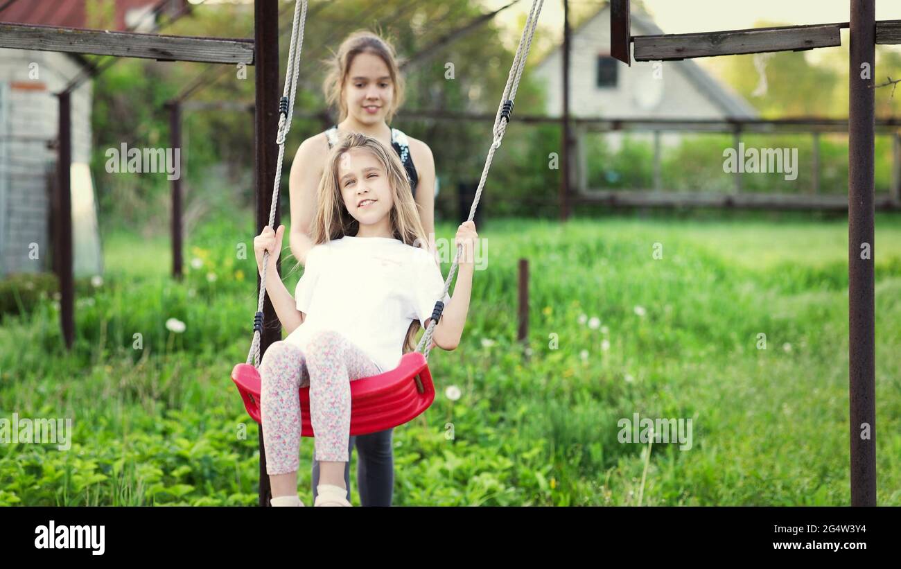 Cheerful children in light clothes ride a street swing in a blooming ...