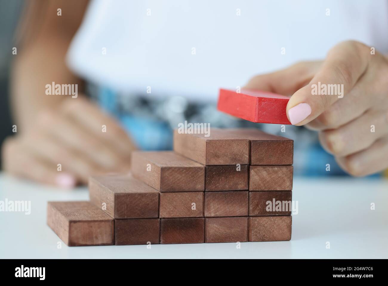 Female hand builds ladder from wooden blocks from above red Stock Photo ...