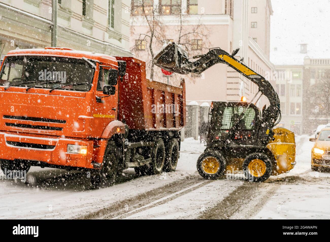excavator load snow in truck. clearing streets of snow during snowfall ...