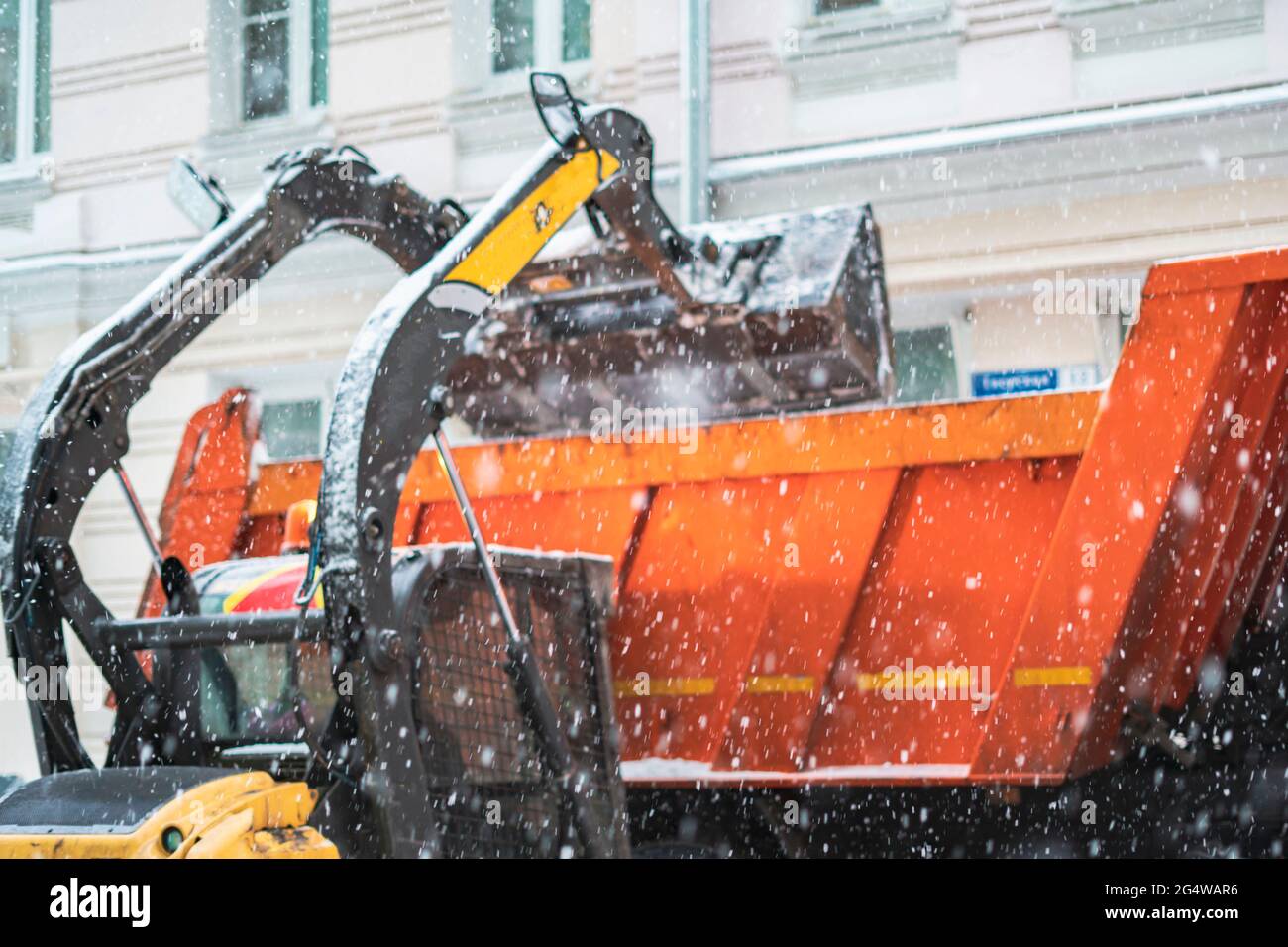 excavator load snow in truck. clearing streets of snow during snowfall ...