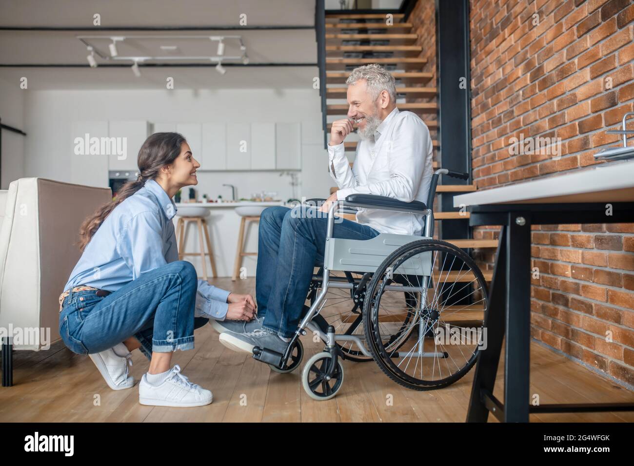 Dark-haired young woman helping her handicapped husband to tie his ...