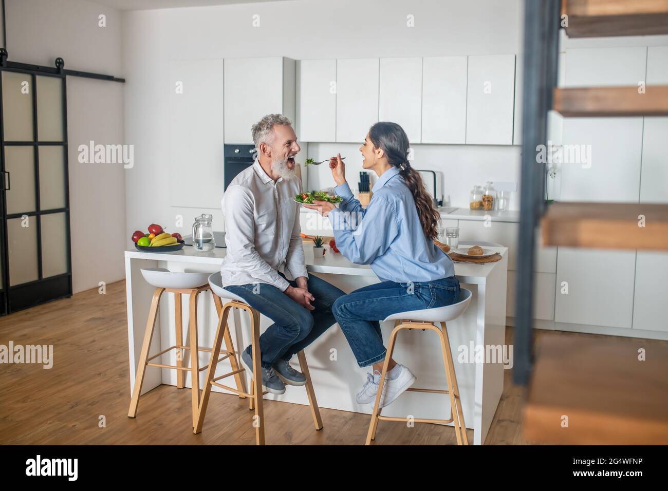 Dark-haired young woman feeding her husband and smiling Stock Photo - Alamy