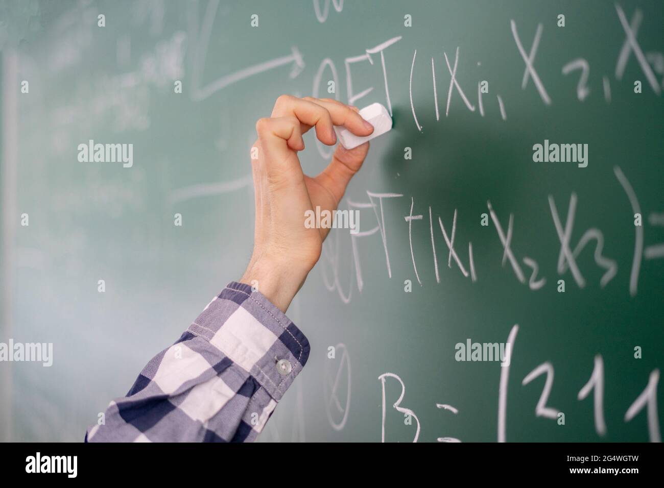 persons hand hold chalk and write mathematic calculations on a board ...