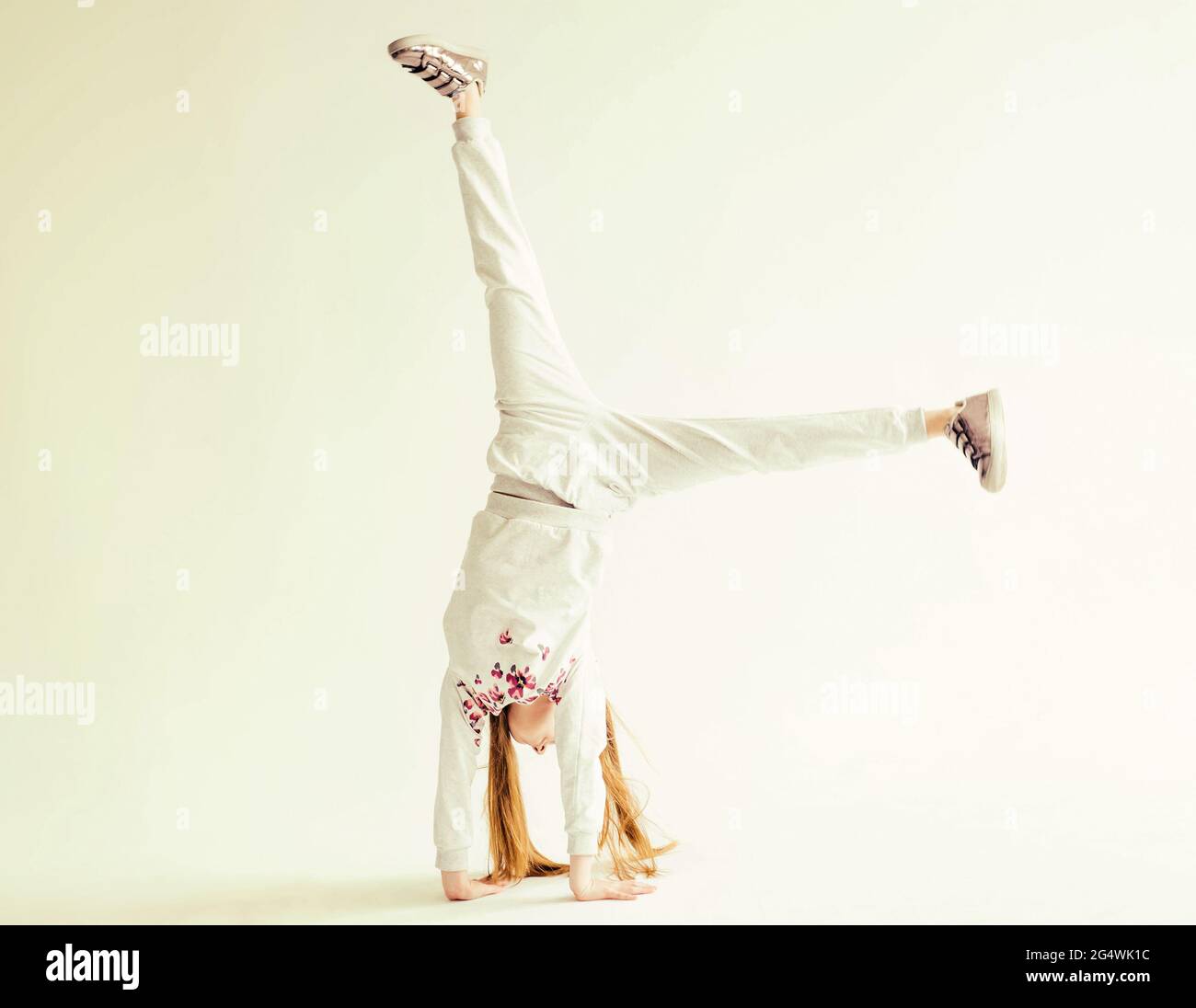 Active little girl in grey sport clothes doing a handstand on white ...