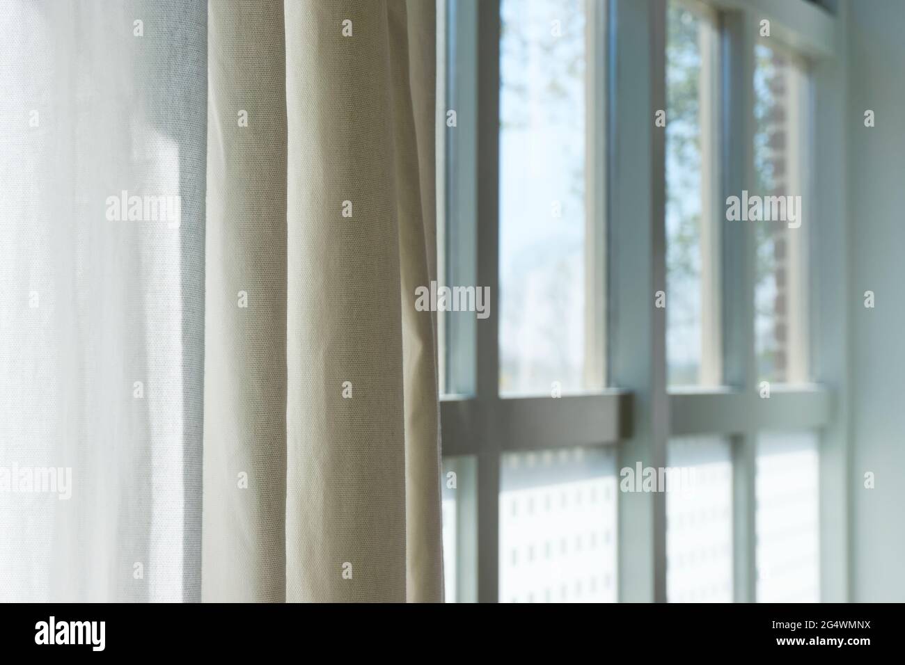 View through light green window frame and half open curtain to the ...