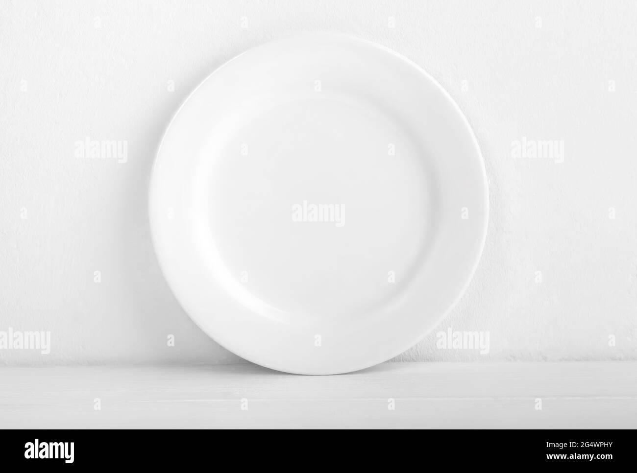 Round clean plate standing near white wall Stock Photo - Alamy