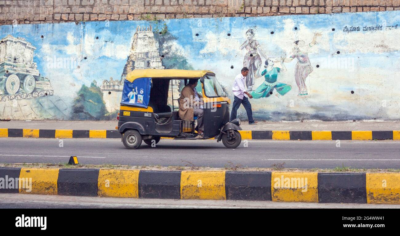 Panorama view of auto rickshaw driving past wall art depicting ancient ...