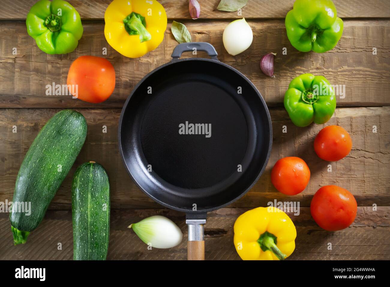 Cast iron frying pan among multi-colored vegetables on a wooden ...