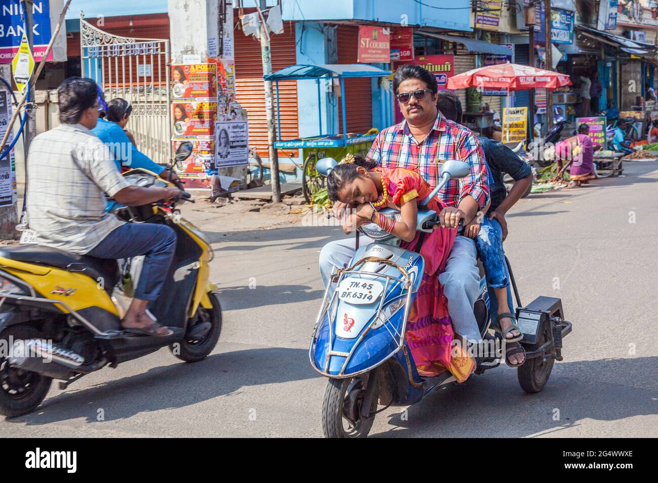 Indian Father driving a three wheel scooter with young daughter slumped ...