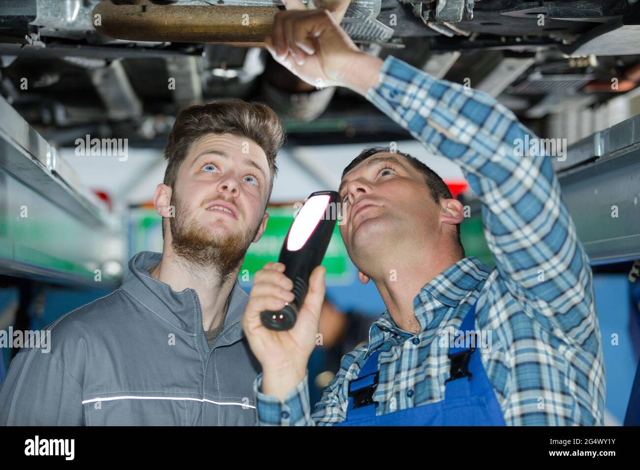 male mechanicsunder lifted car at garage Stock Photo - Alamy