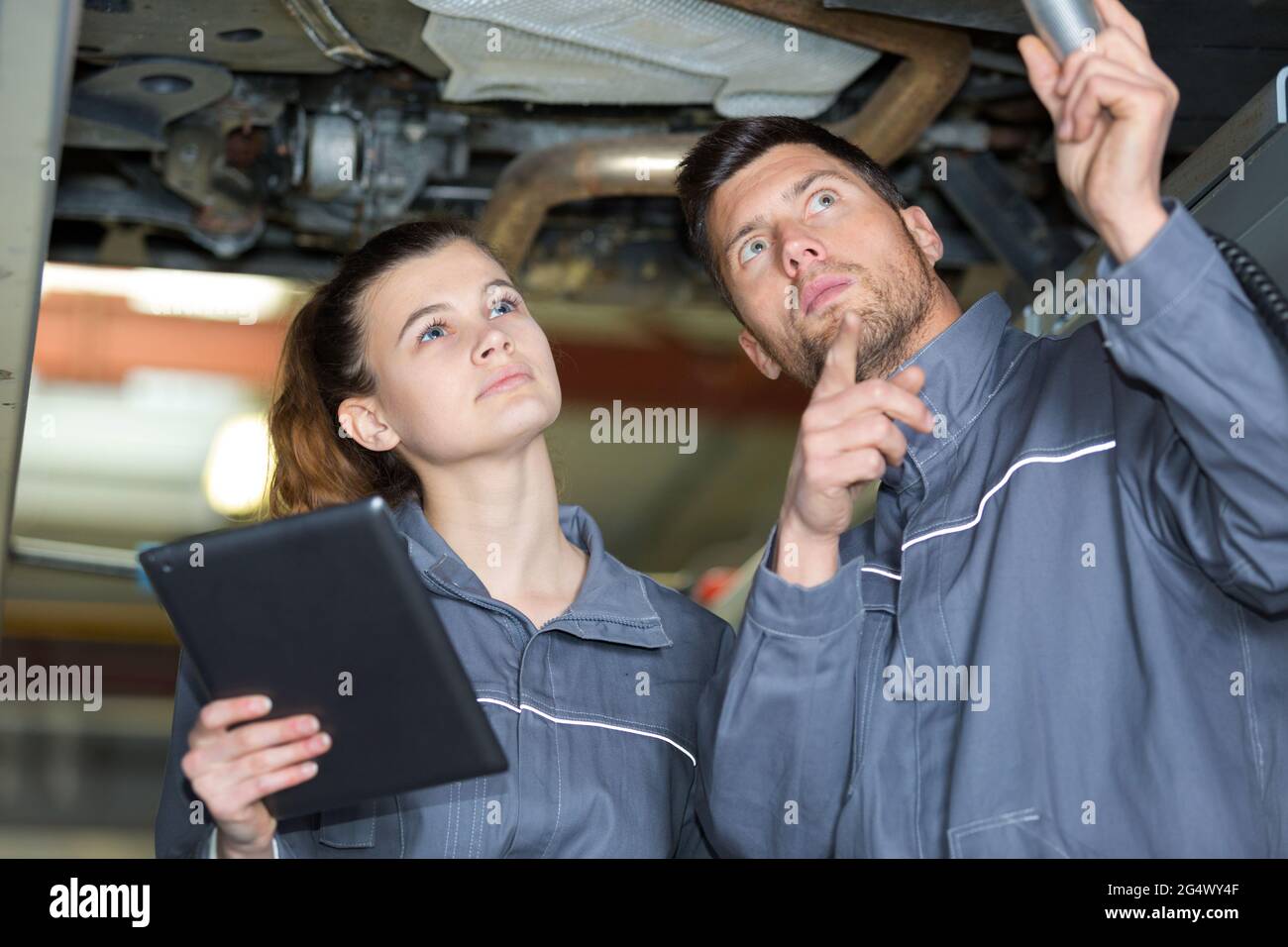mechanic pointing at car leaks underneath Stock Photo - Alamy