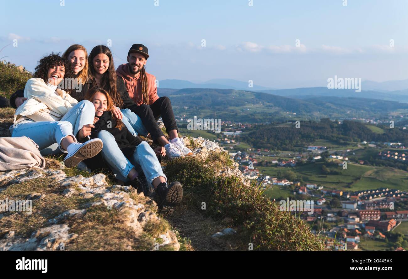 Happy male and female friends sitting on cliff Stock Photo - Alamy