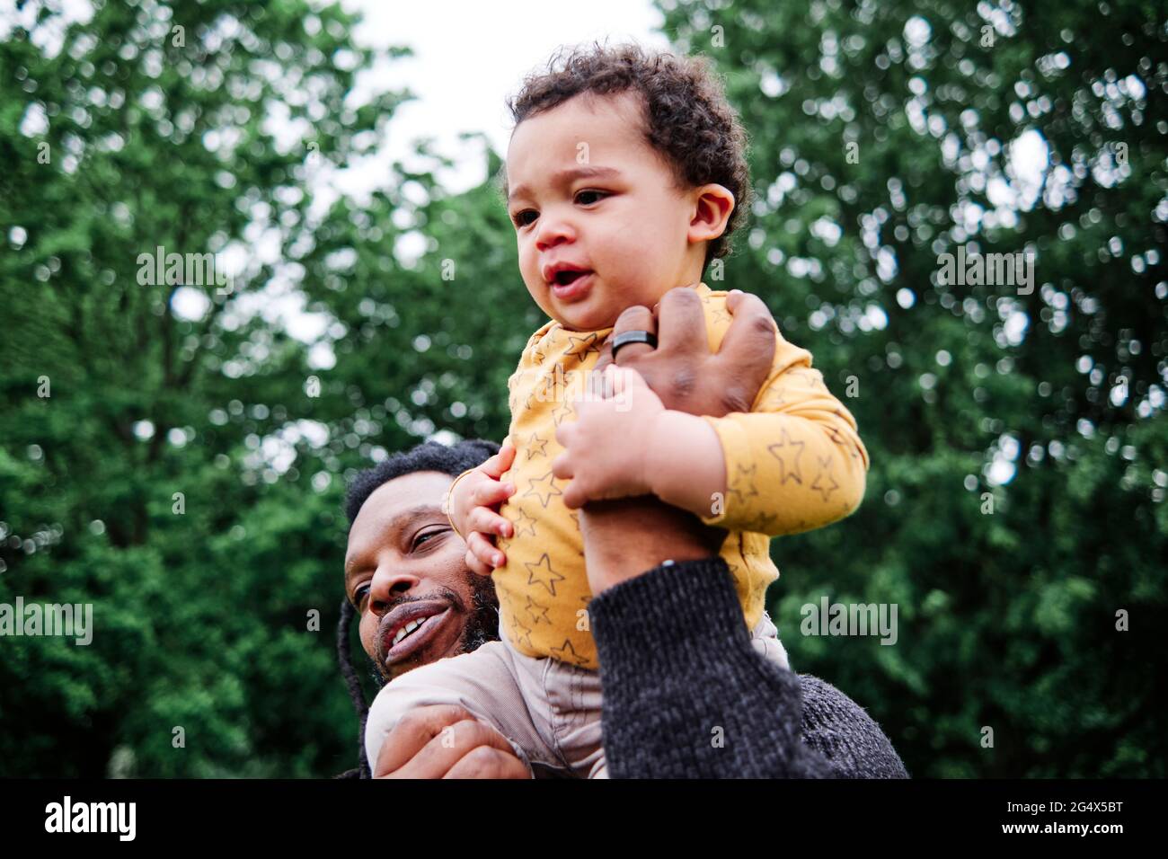 Son sitting on father's shoulder at park Stock Photo - Alamy