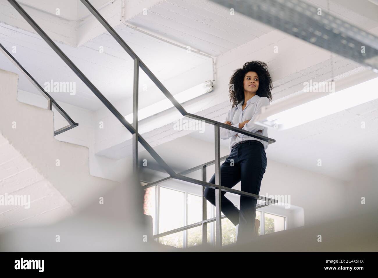 Female professional with arms crossed contemplating while leaning on ...