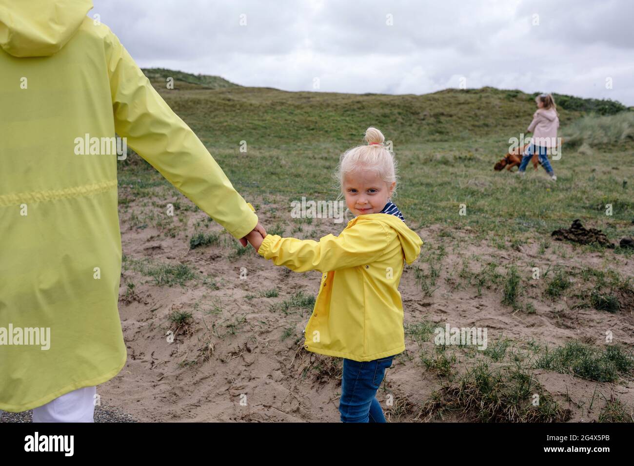 Cute daughter holding hand of mother while walking on hill Stock Photo ...