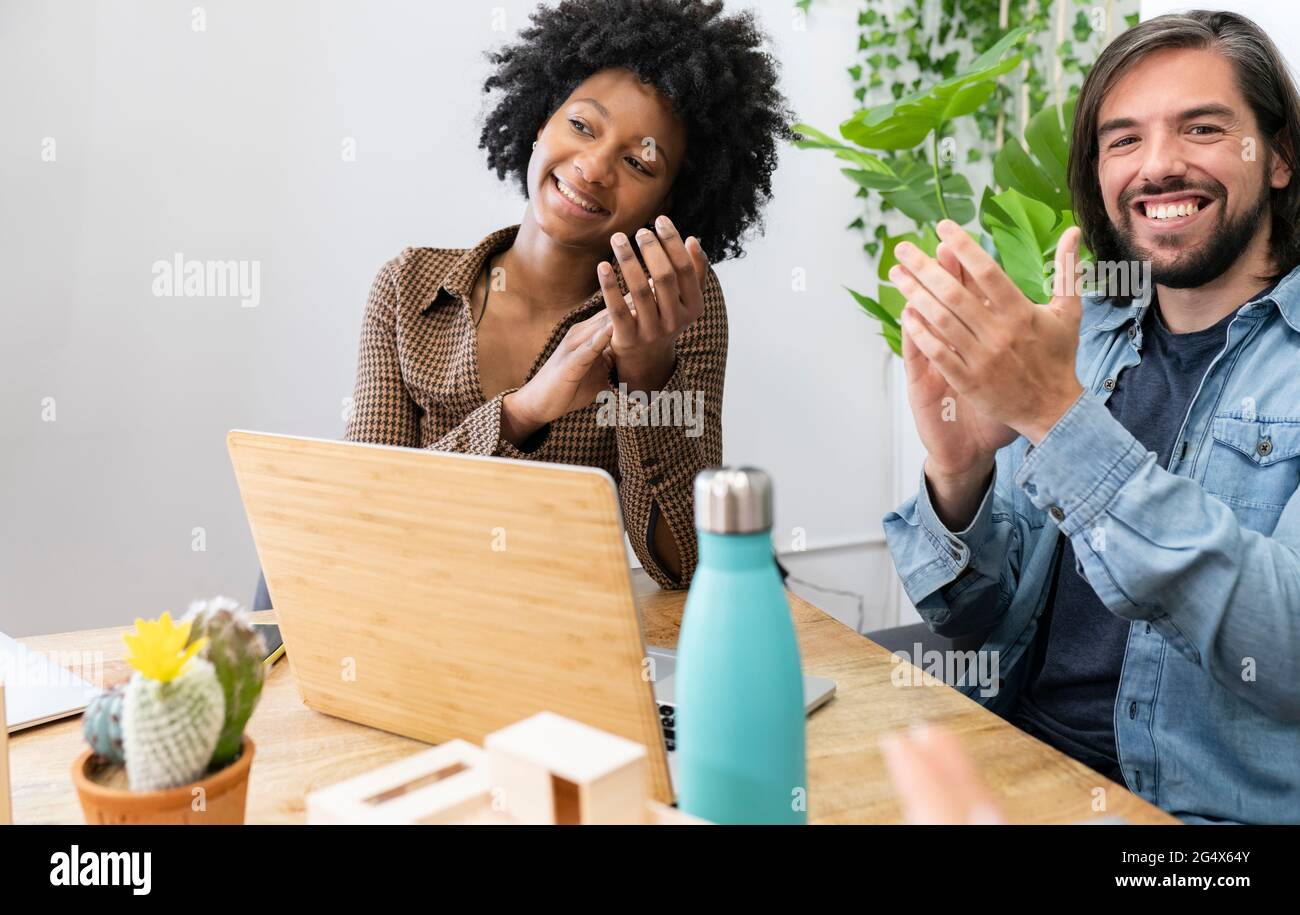 Happy male and female professional clapping while sitting at desk ...