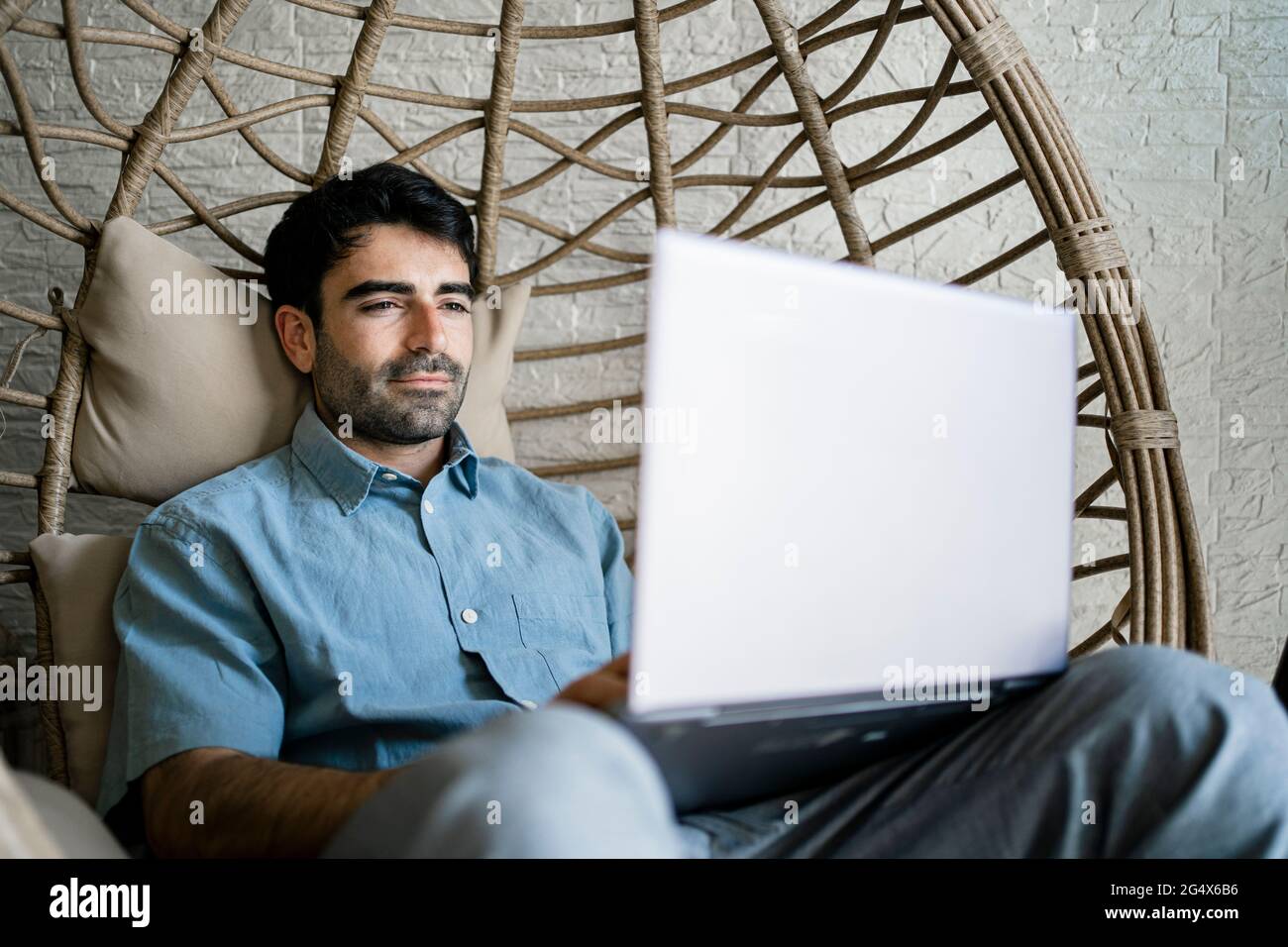 Male freelancer using laptop while sitting on chair swing in cafe Stock ...