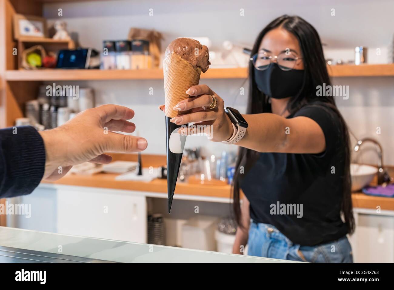 Female employee giving ice cream to customer at store during COVID-19 ...