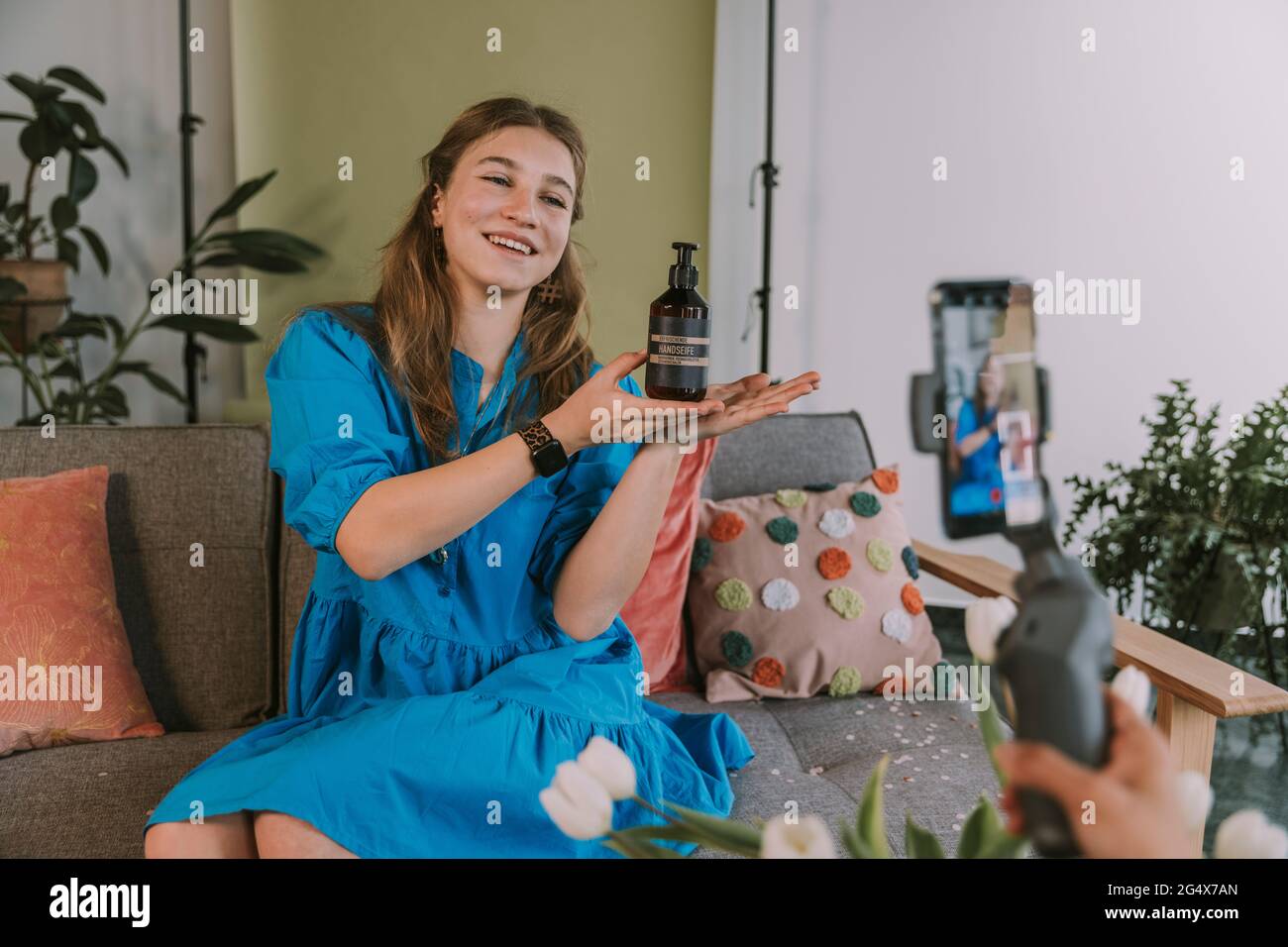 Smiling teenage girl presenting beauty product while vlogging at home ...
