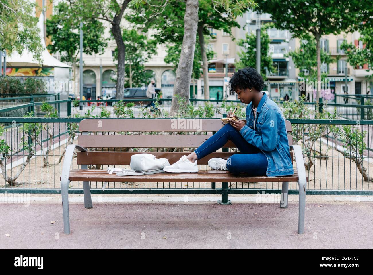 Afro woman writing while sitting on bench Stock Photo - Alamy