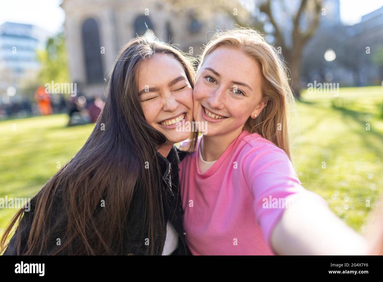 Happy women with cheek to cheek standing in public park Stock Photo - Alamy