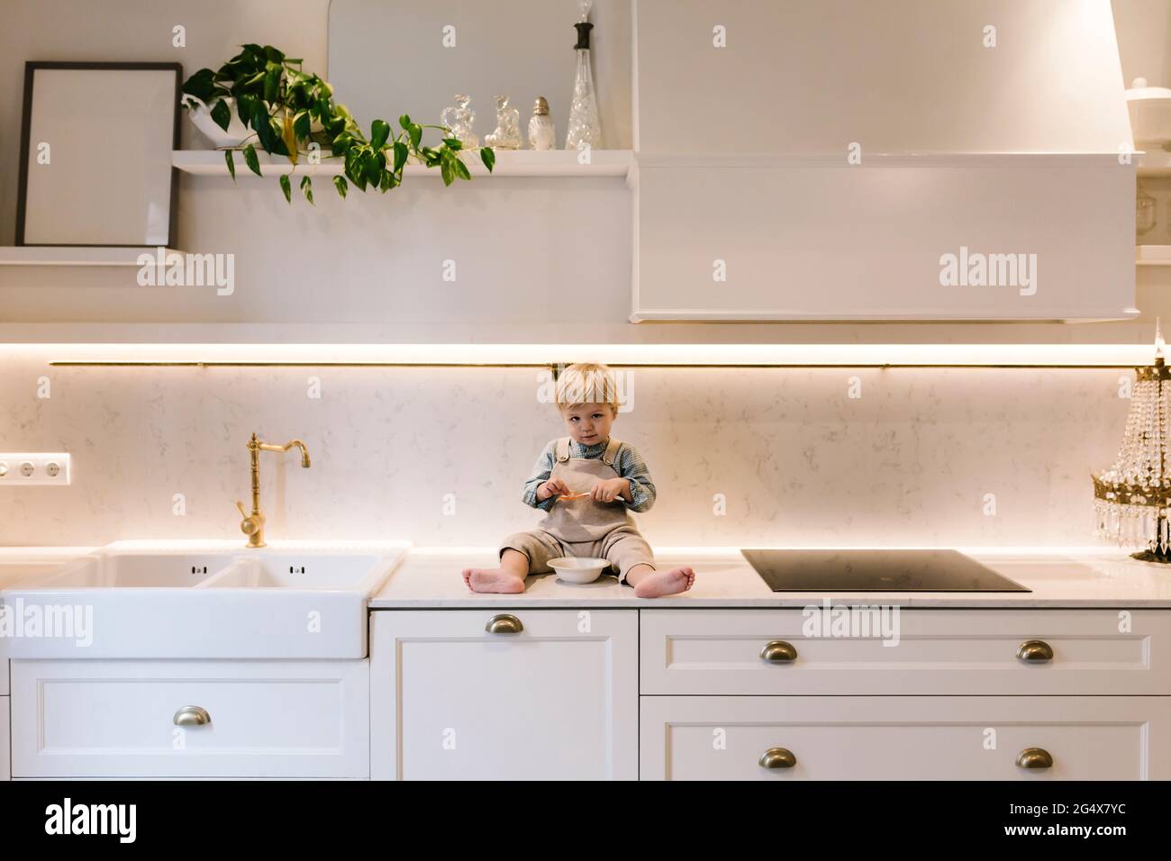 Innocent boy having food while sitting on kitchen counter at home Stock ...