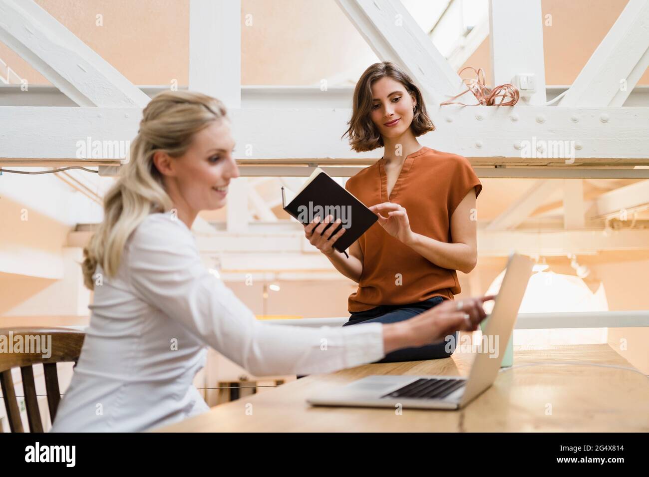 Young female professional looking at coworker pointing on laptop while ...