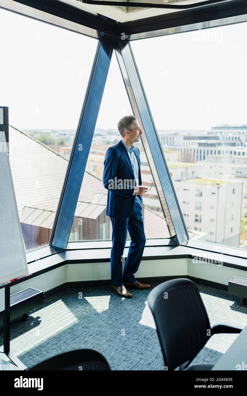 Male entrepreneur standing in board room while looking through window ...
