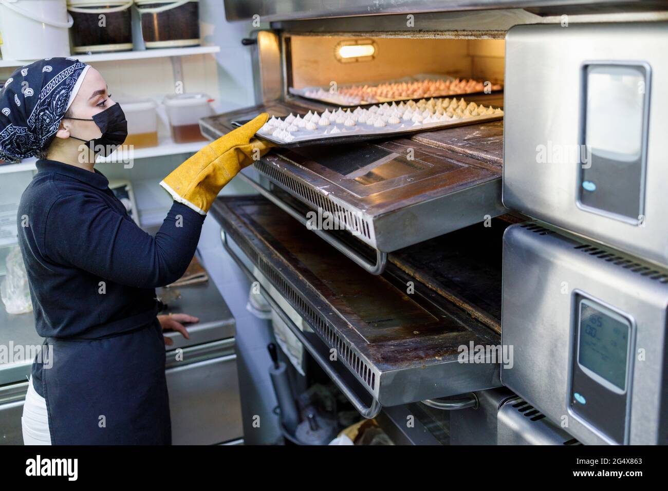 Female baker taking out tray from oven at commercial kitchen Stock ...