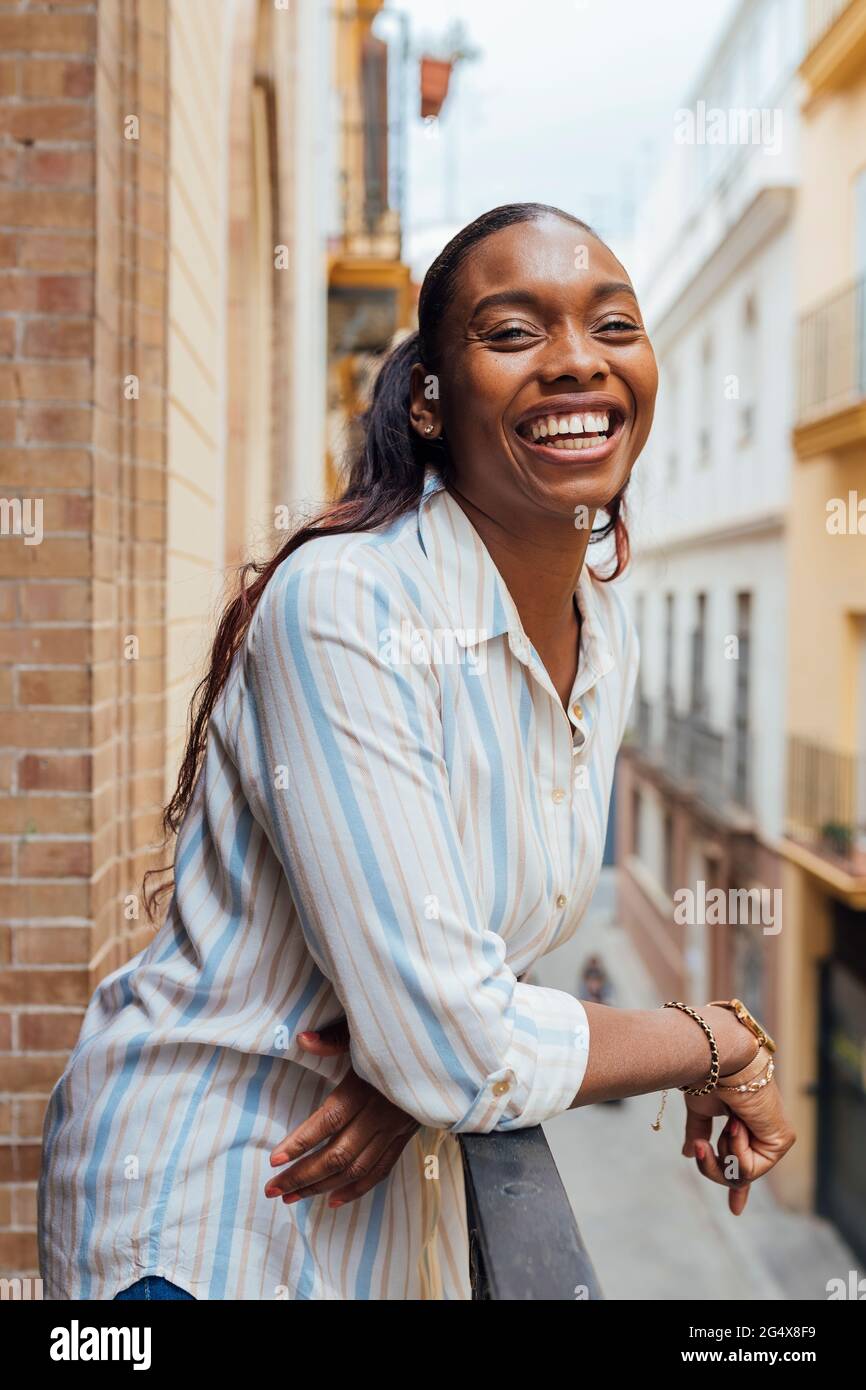 Cheerful woman leaning on railing in balcony Stock Photo - Alamy