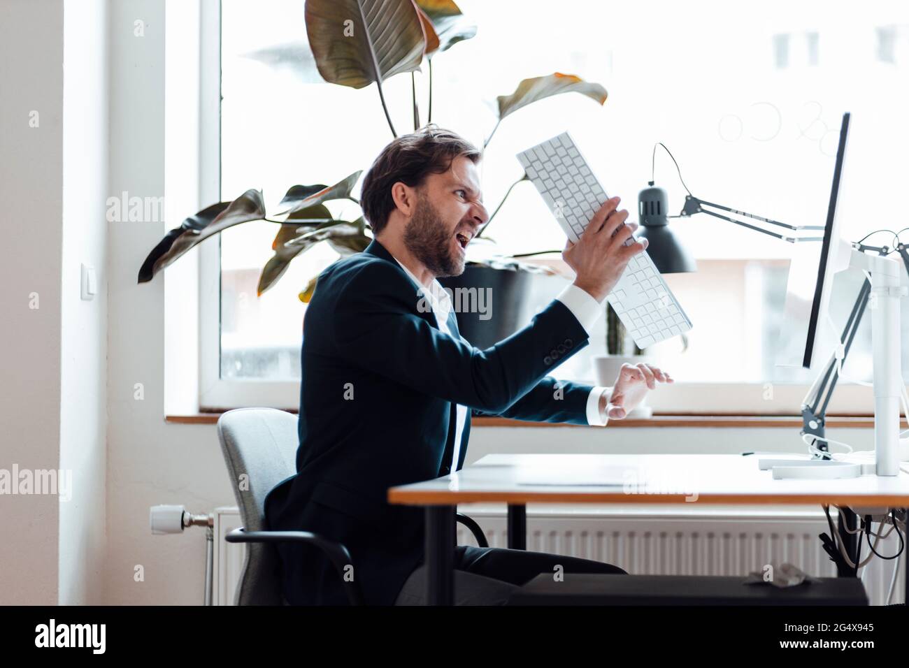 Angry businessman holding computer keyboard while sitting by desk Stock ...