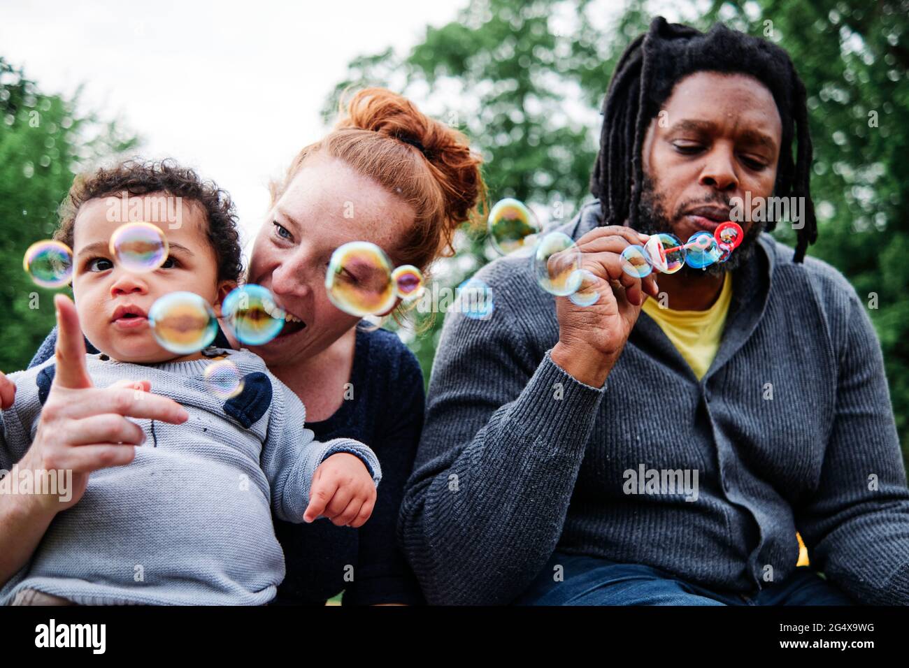 Father blowing bubbles while playing with family at park Stock Photo ...