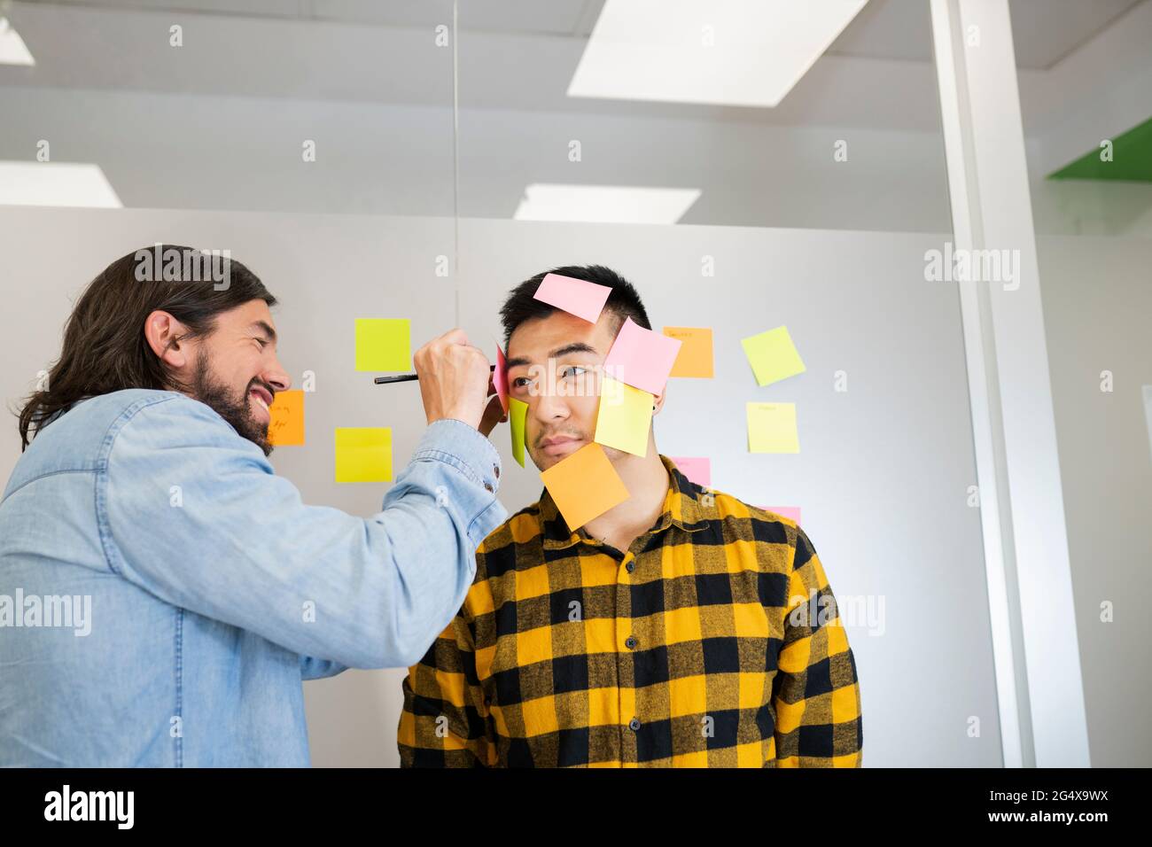 Mischievous male professional writing on adhesive notes sticking on ...