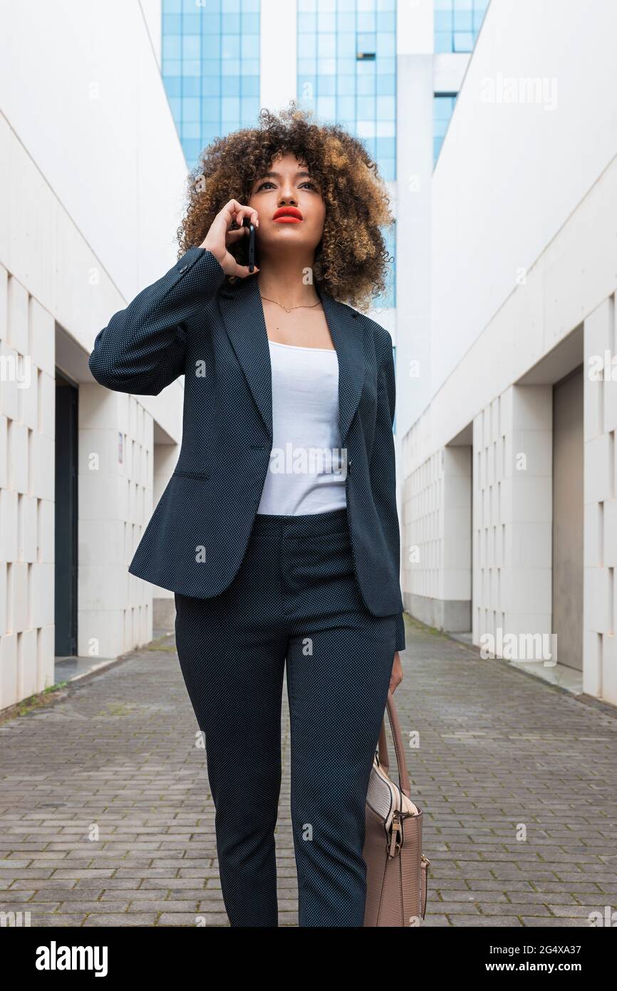 Businesswoman with purse talking on smart phone while walking amidst ...
