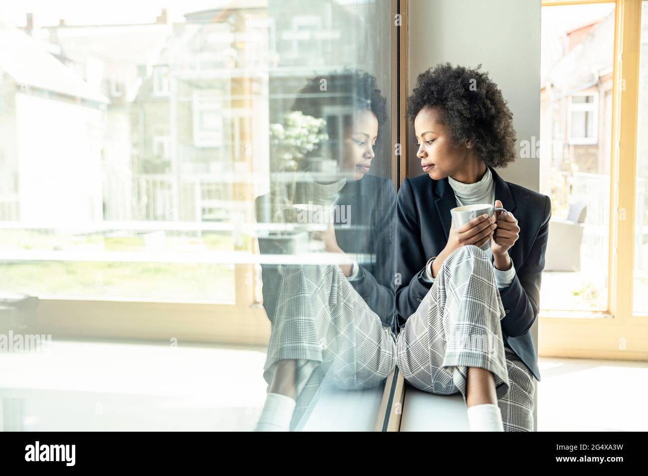 Female professional looking down while sitting on window sill at office ...