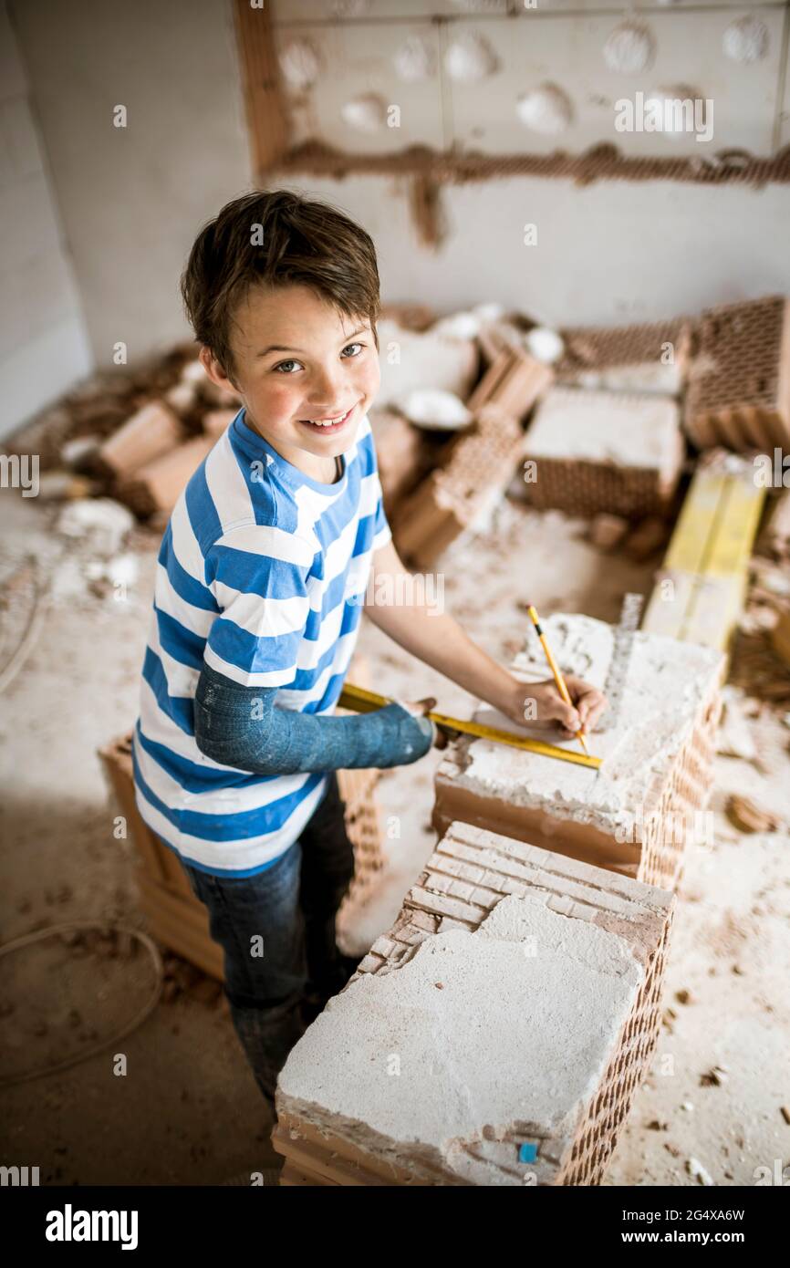Smiling boy measuring brick while standing at house during renovation ...