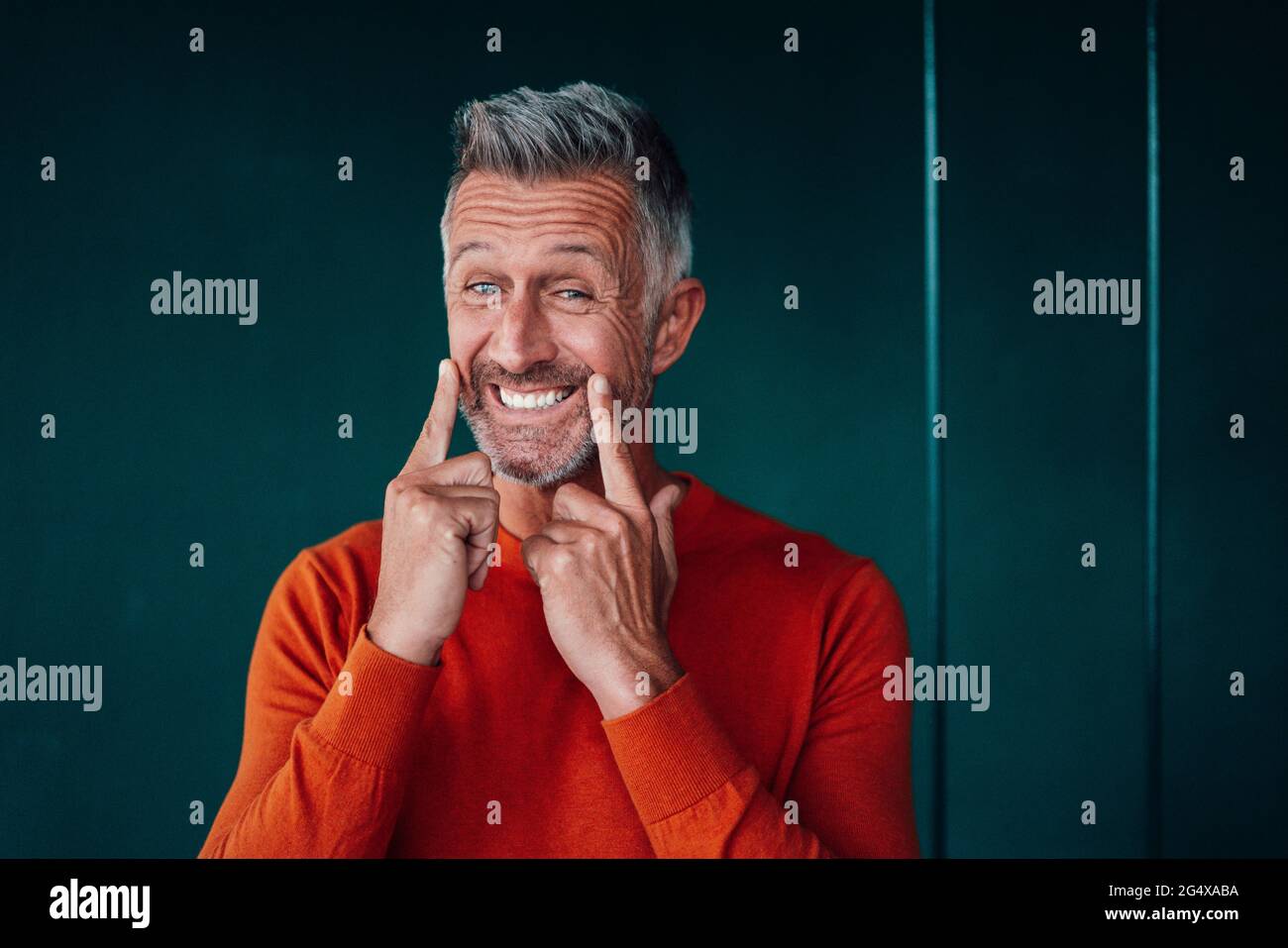 Smiling man touching cheeks in front of wall Stock Photo - Alamy