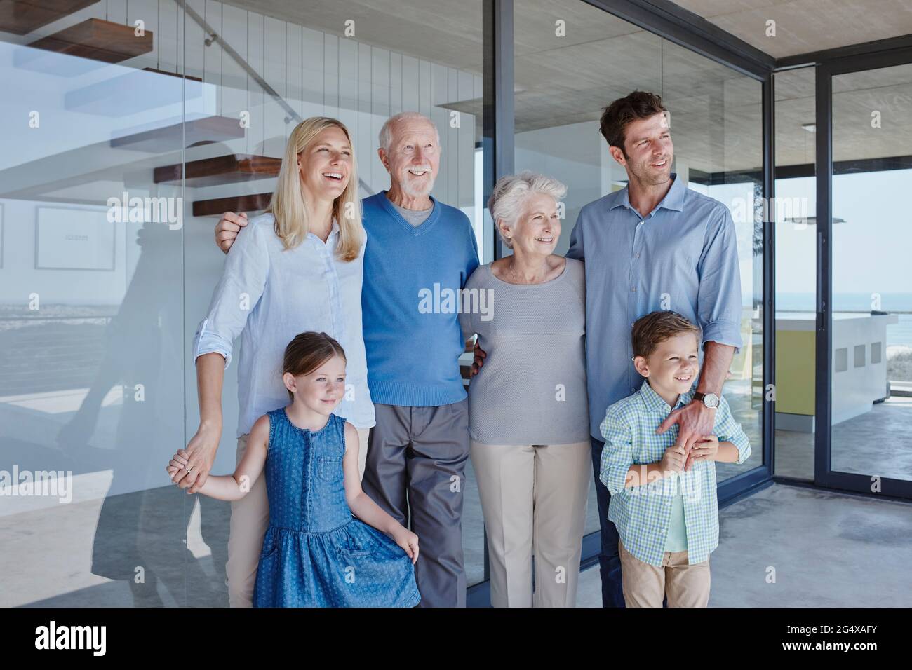 Smiling multi-generation family standing together in front of glass ...