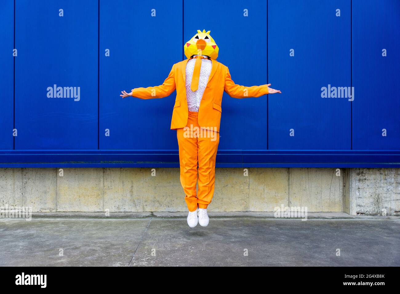 Man wearing vibrant orange suit and bird mask levitating in front of ...