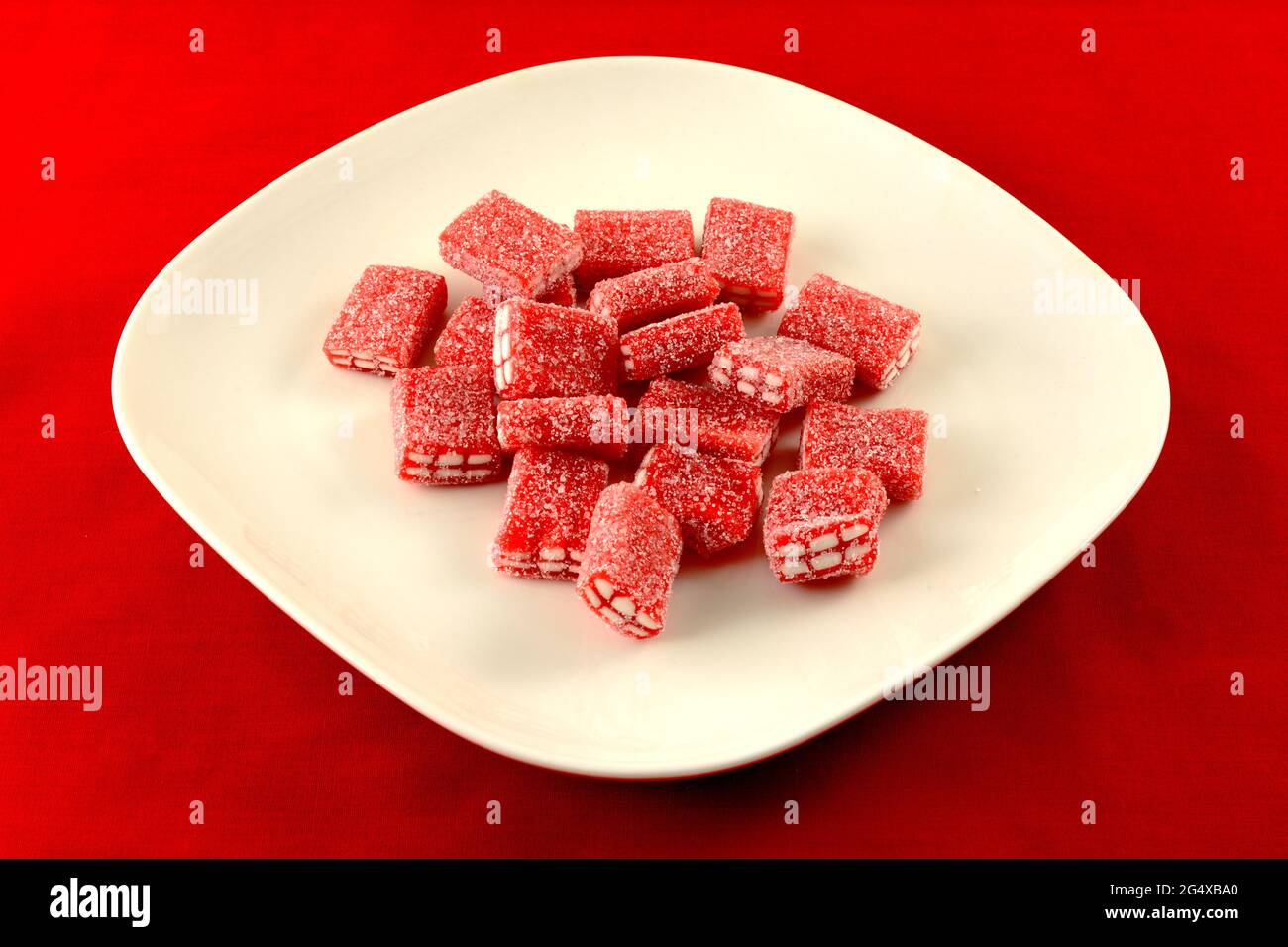 Strawberry gummy brick candy coated in sour sugar on white plate on red ...