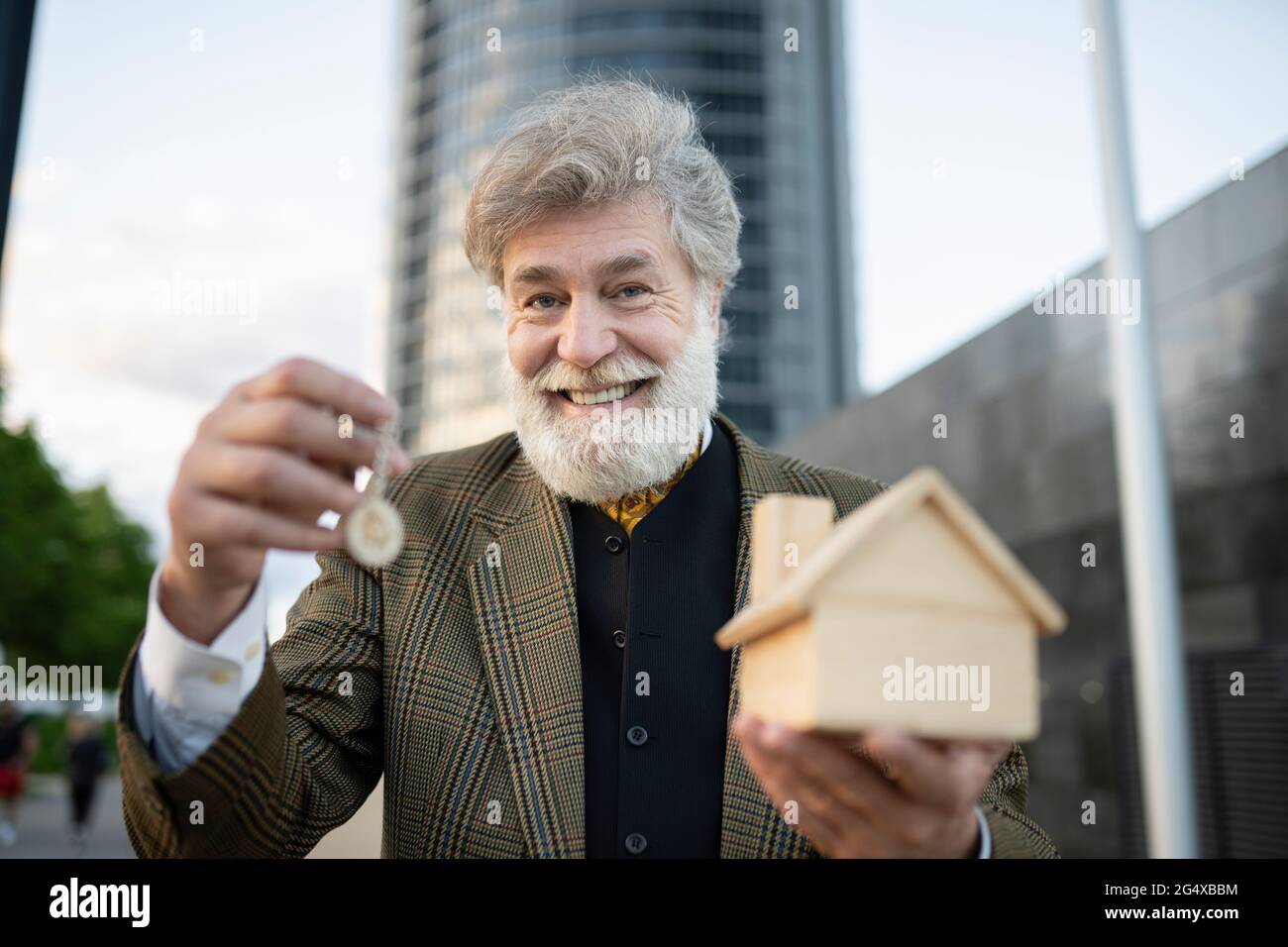 Smiling male realtor offering model house and key in city Stock Photo ...