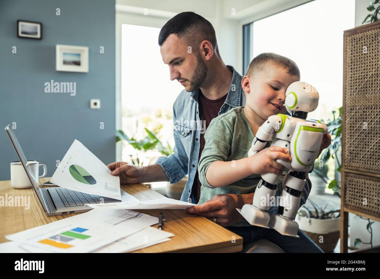 Boy playing with robot sitting while businessman analyzing graph at ...