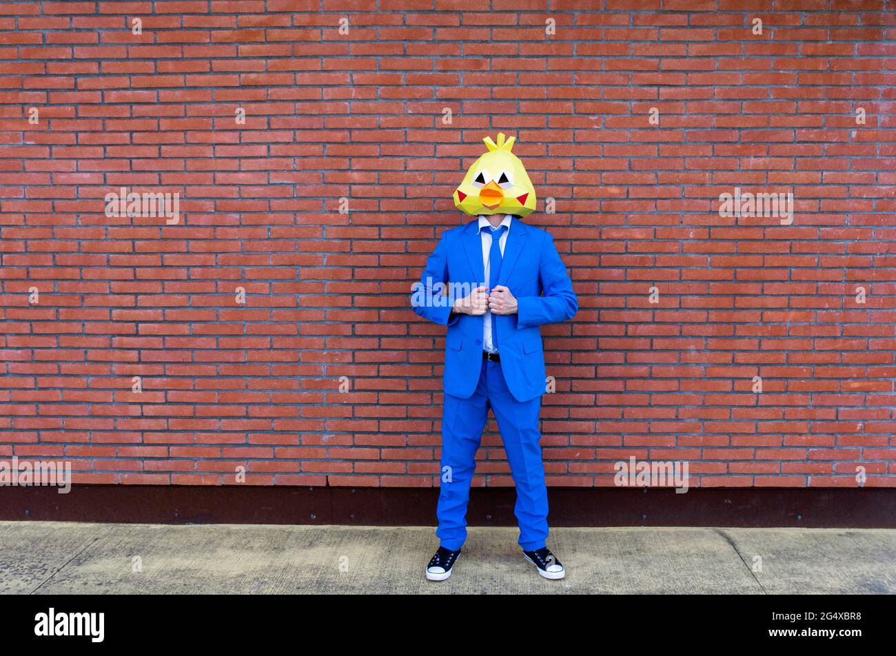 Man wearing vibrant blue suit and bird mask standing in front of brick ...