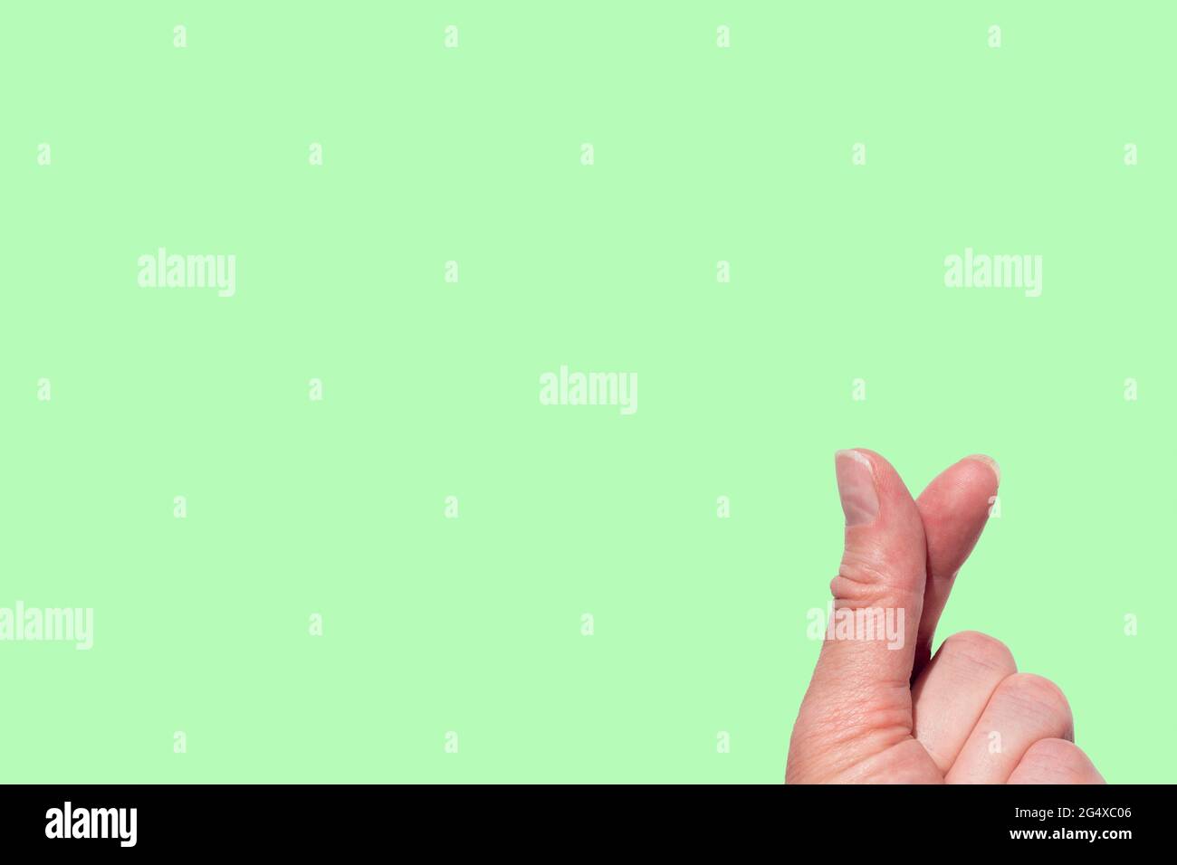 A hand making a heart shape with two fingers on a mint green background ...