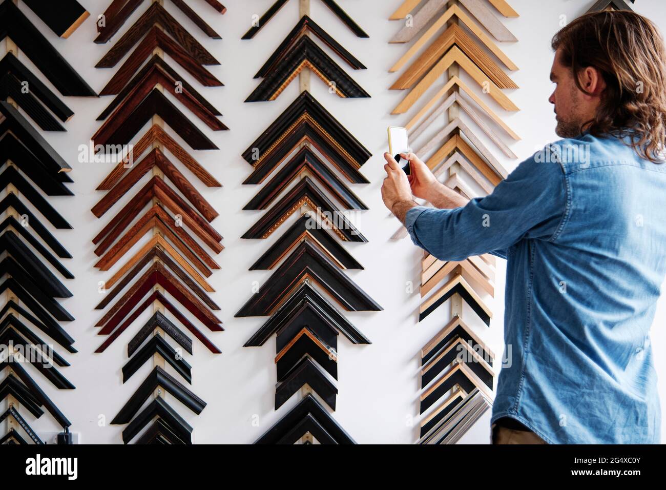 Craftsman photographing frame borders through smart phone in workshop ...