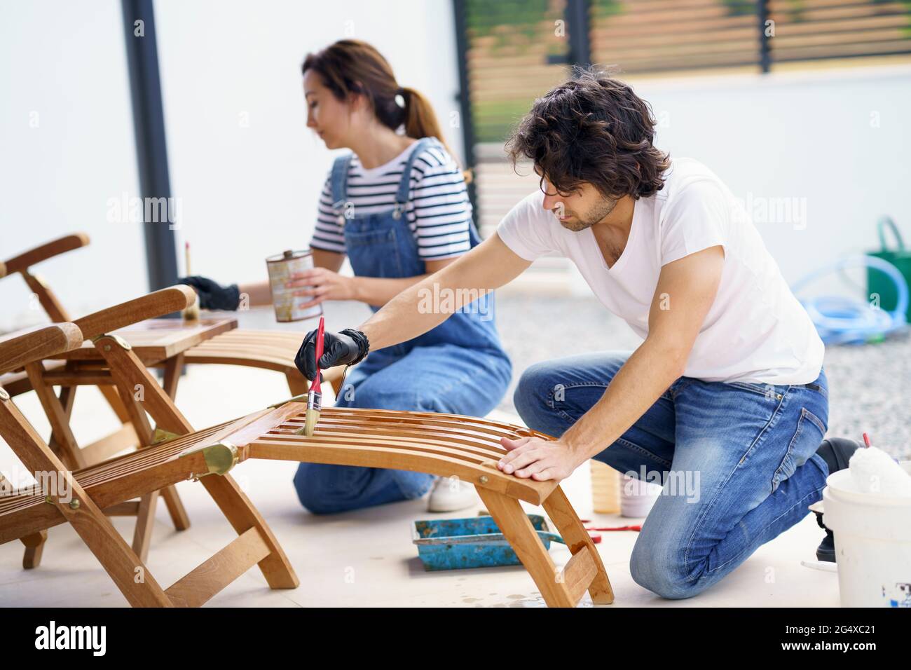 Mid adult boyfriend and girlfriend painting deck chair in new house ...